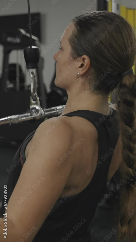 Vertical video. Young woman performs wide-grip seated lat pulldowns ...