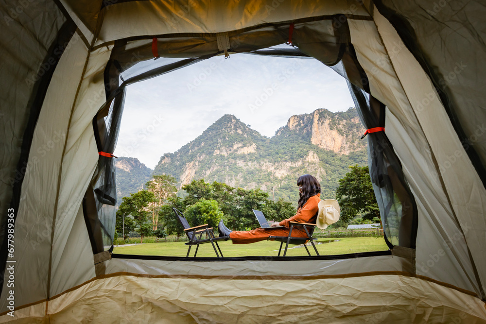 Young woman sitting near tent with bucket hat hanging on camping chair ...