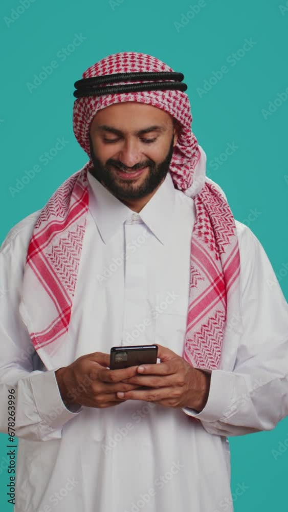 Vertical video Cheerful person messaging on phone, wearing islamic ...
