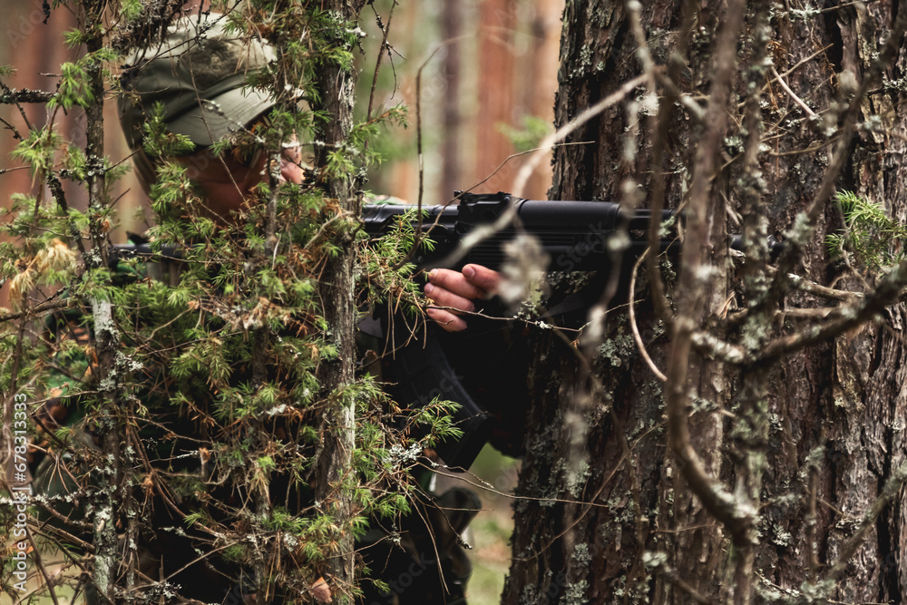Soldier man shooting from weapon from behind tree, dressed in military ...