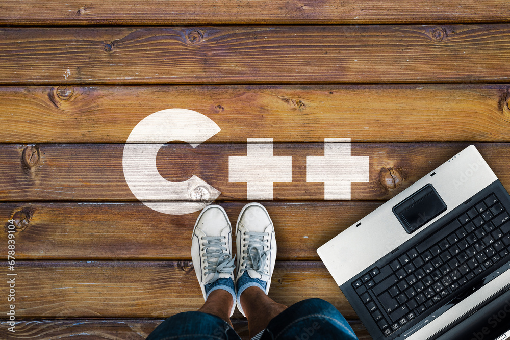 Legs in sneakers standing next to laptop and c++ on wooden floor. C++ ...