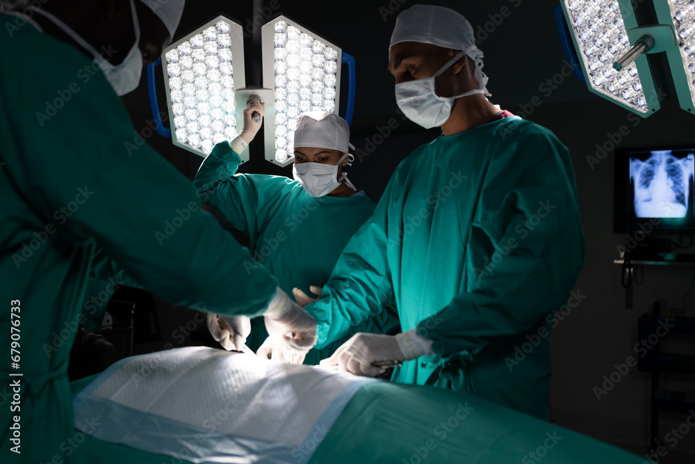 Diverse surgeons wearing surgical gowns operating on patient in ...