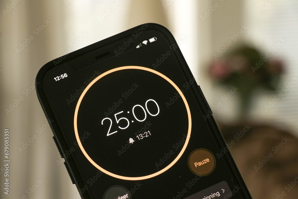 A phone with a black and orange 25-minute timer to study with the pomodoro method on a blurry ...