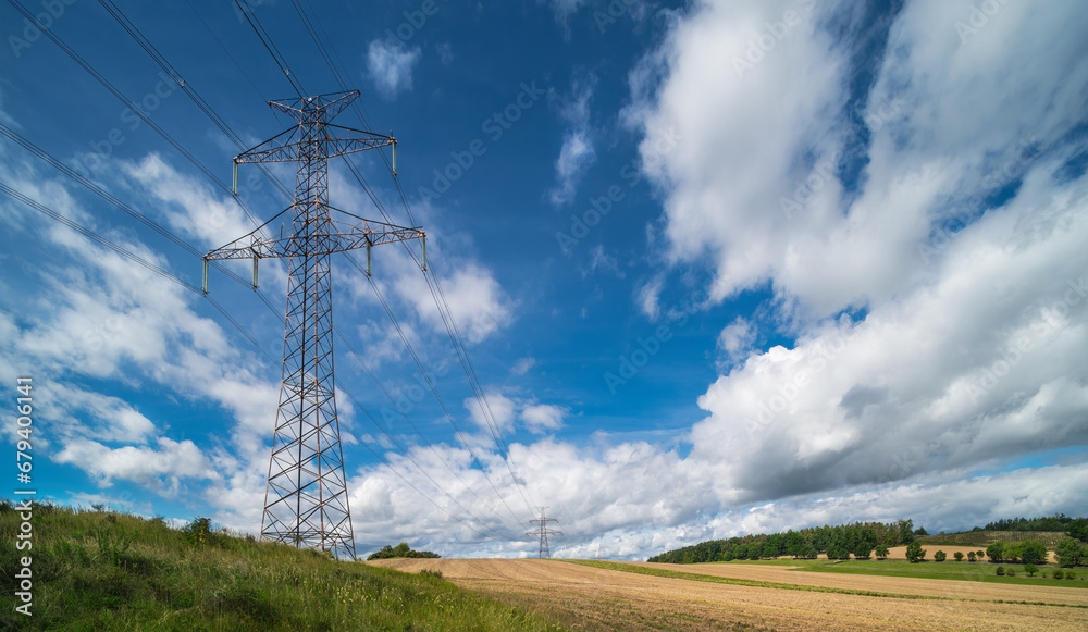 Overhead power line pylon in summer landscape with blue sky and puffy ...