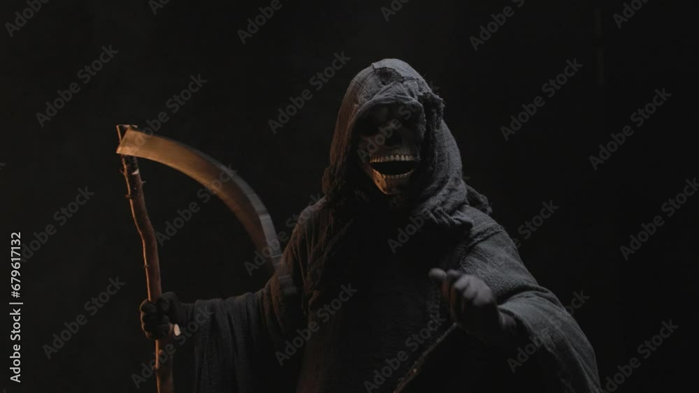 Grim reaper preparing his scythe. Studio portrait on black background ...
