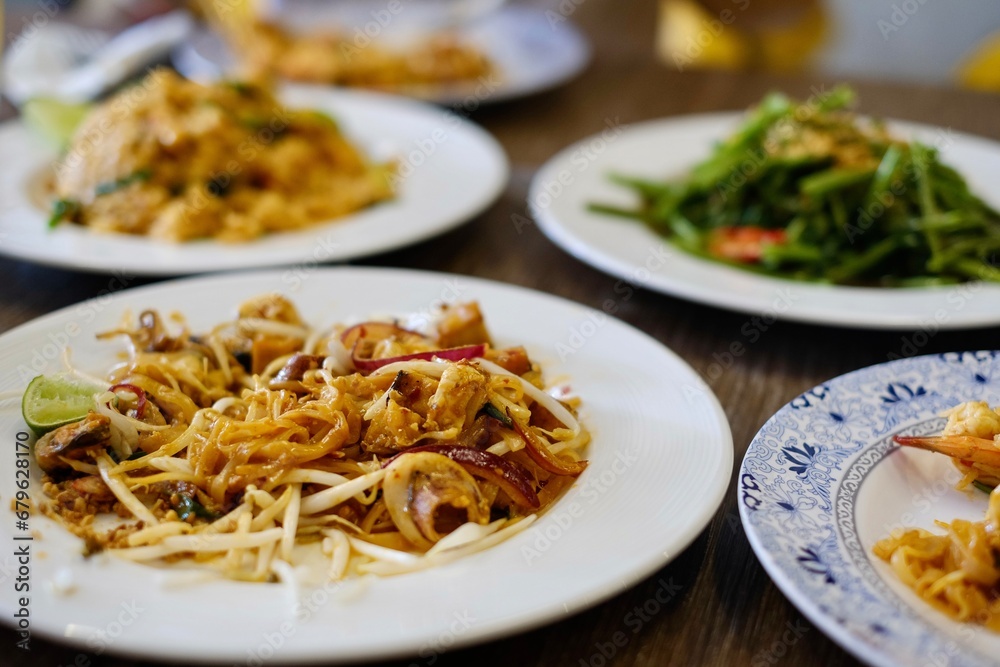 A full table of Thai dishes: seafood pad thai, chicken tom yum fried ...