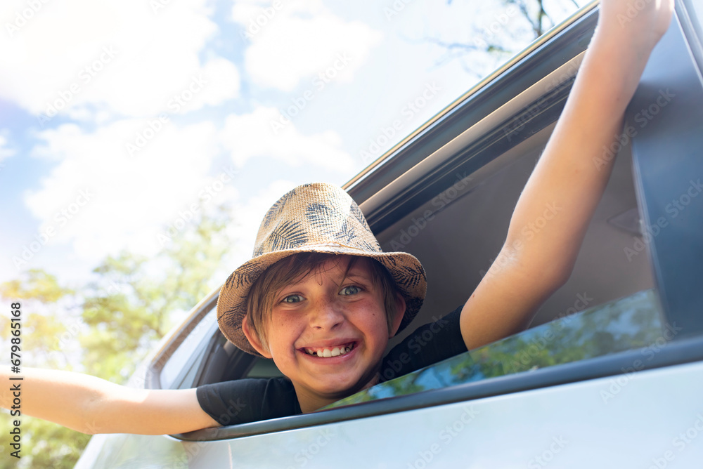 emotional boy waves his hands from the car window. happy child in a hat ...