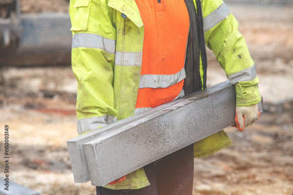 groundworker in orange and yellow hi-viz carrying heavy concrete edging ...
