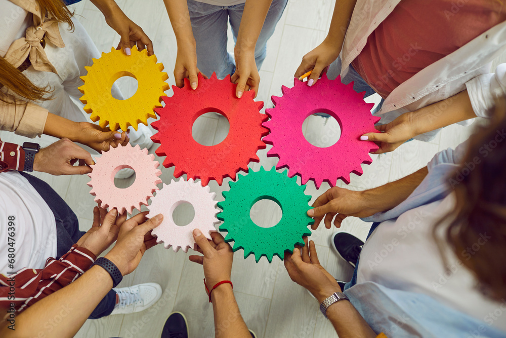 Young people hands connect multy colored cogwheels to make gear. Symbol ...