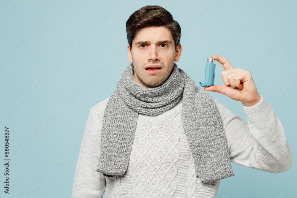 Young sad ill sick man wear gray sweater scarf use asthma inhaler look ...