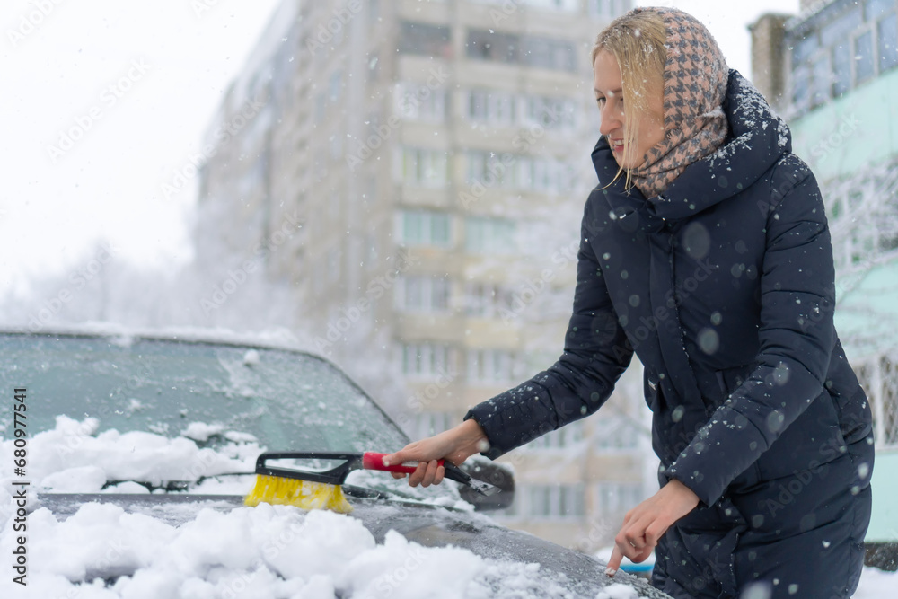 Portrait of a young woman removing snow from the roof and windows of a ...
