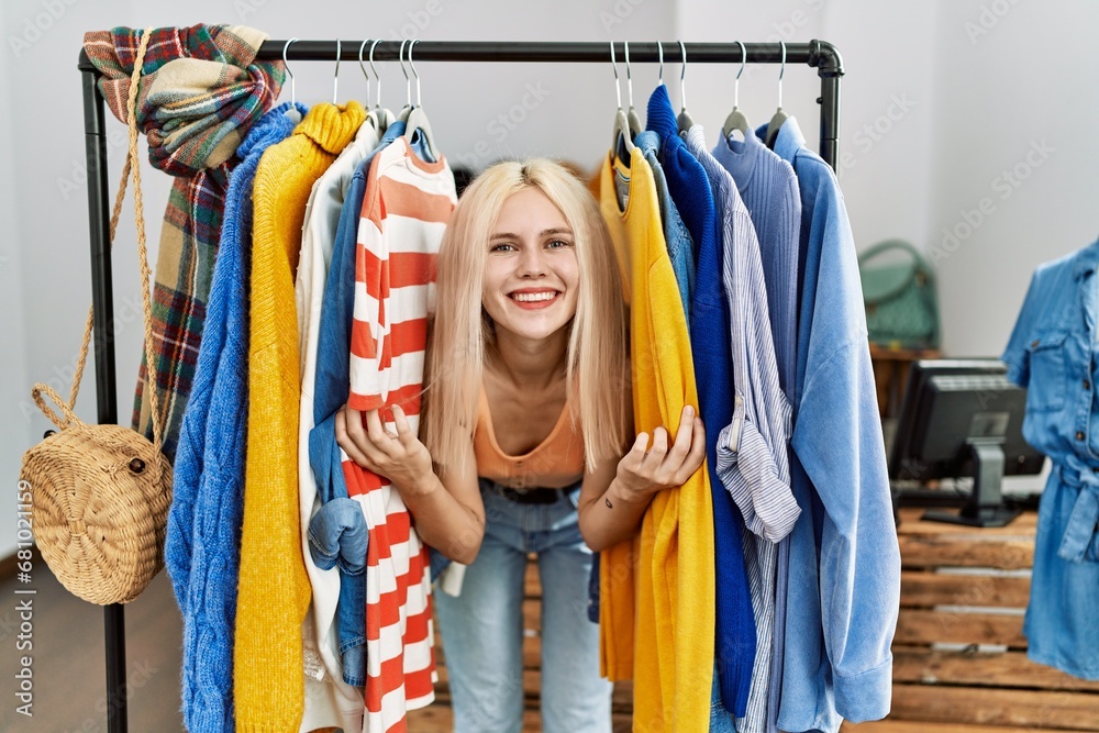 Young blonde woman customer smiling confident between clothes at ...