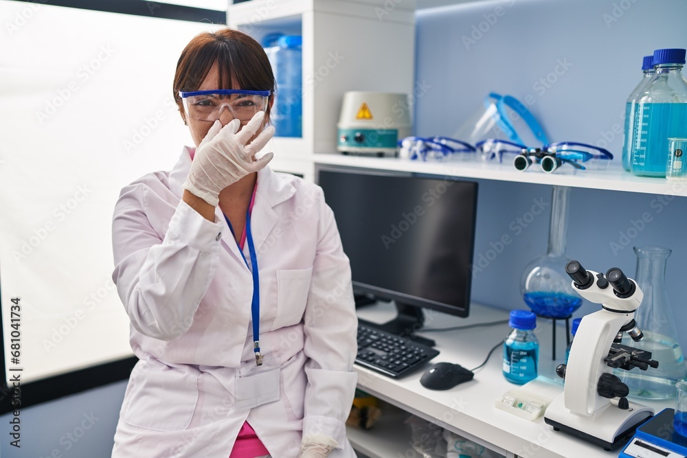 Young brunette woman working at scientist laboratory smelling something ...