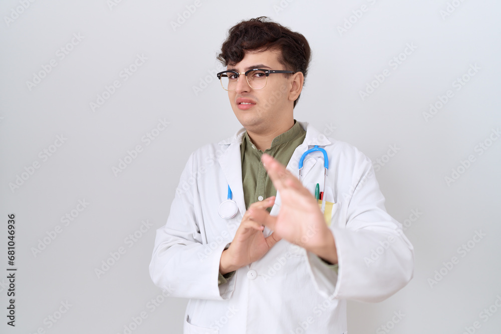 Young non binary man wearing doctor uniform and stethoscope disgusted ...