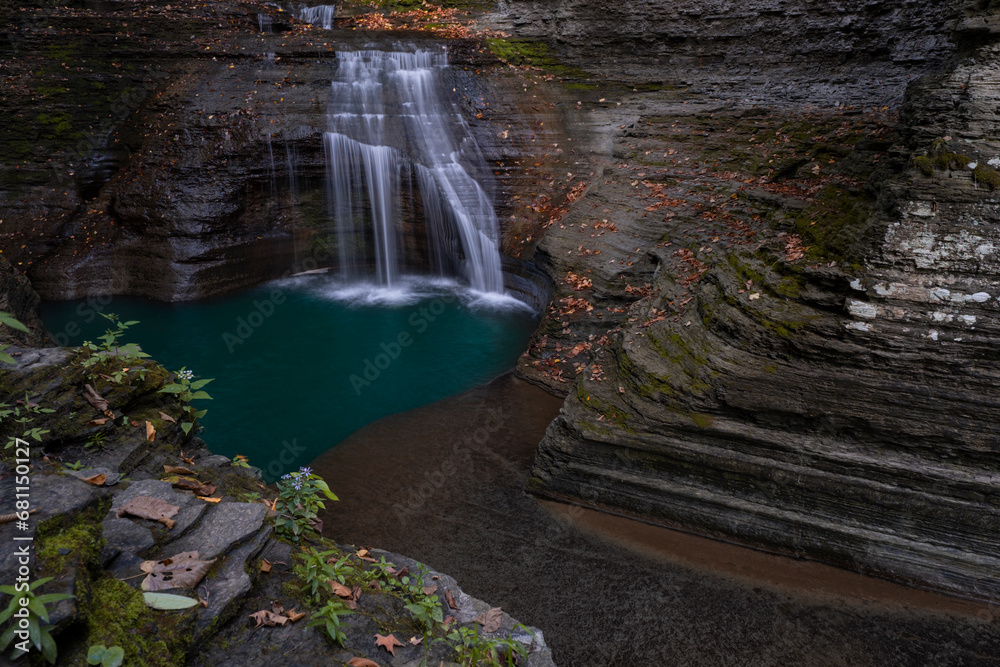 Waterfall in a deep gorge surrounded by forest trees and colorful ...