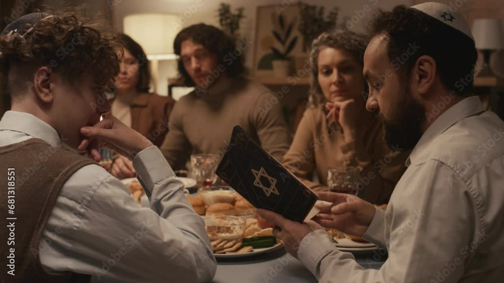 Medium shot of Jewish man in kippah sitting at Hanukkah dinner with ...