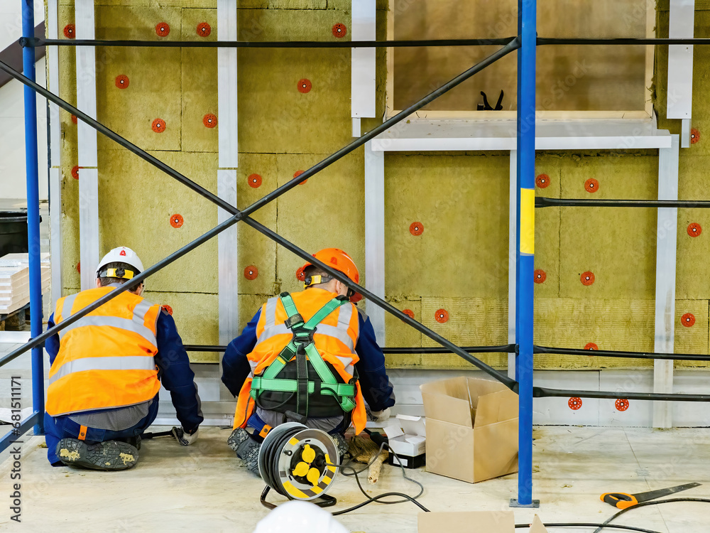 Builders at work. Men install insulation on wall building. Builders ...