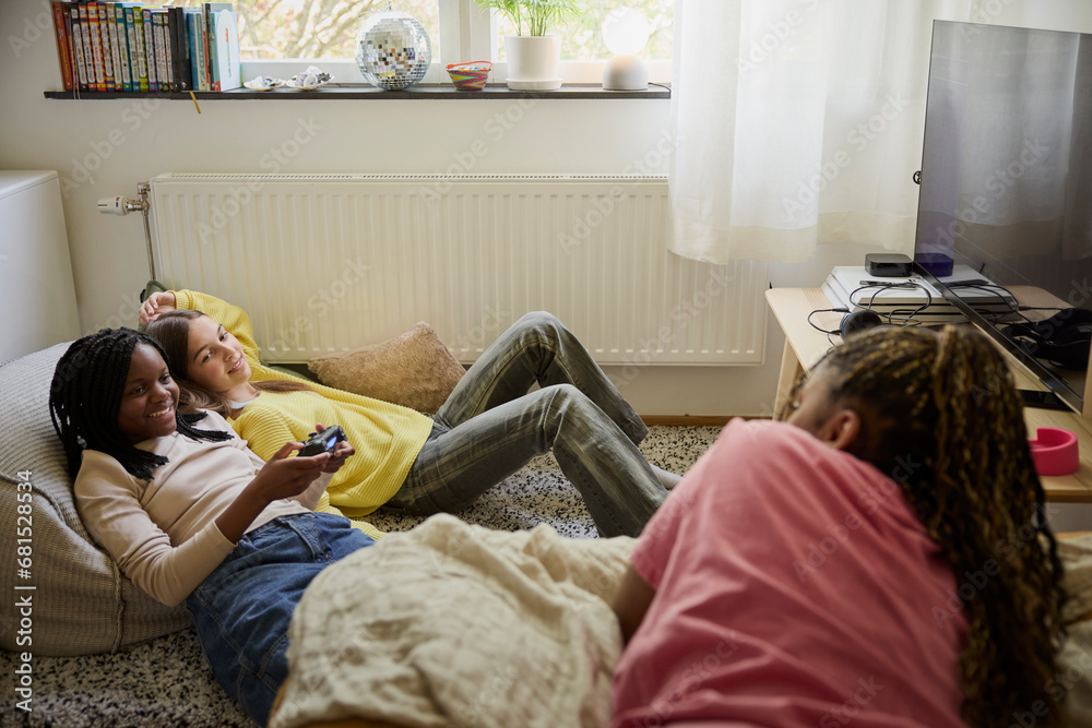 Smiling teenage girl holding game controller while lying down with ...