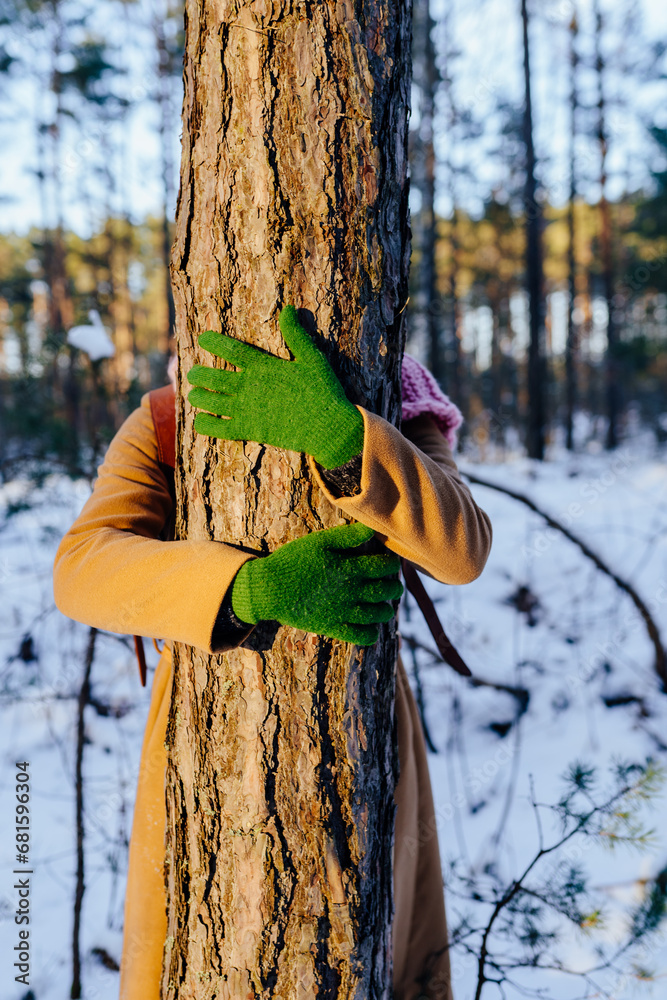 Nature lover hugging trunk tree with green mittens in winter woods ...
