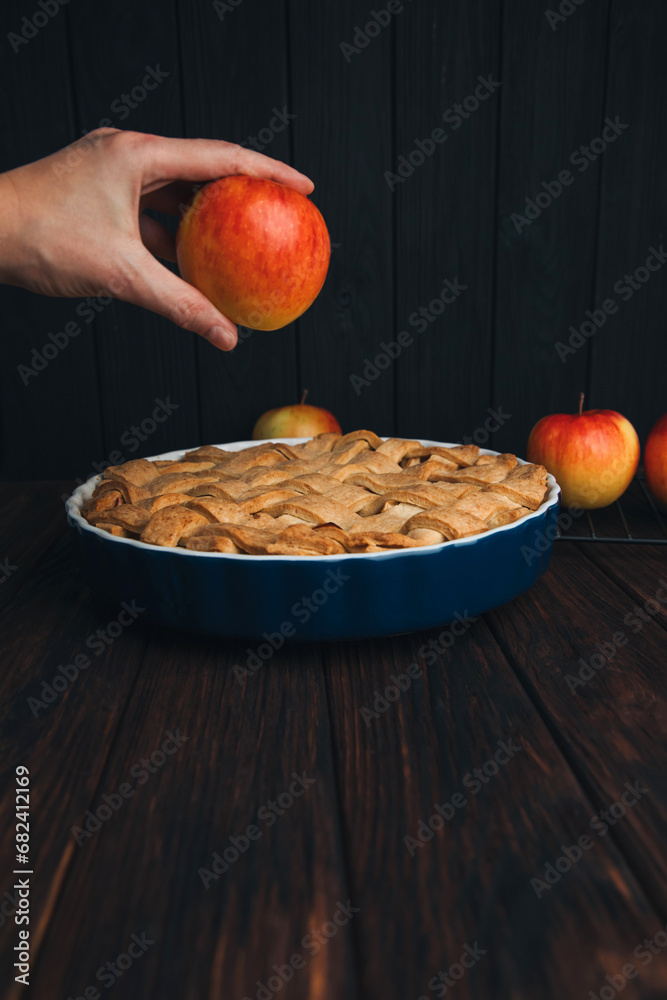 Apple pie in blue form on a dark wooden background and woman's hand ...