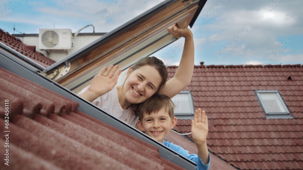 Happy mother and her son open attic windows, embrace the view outside ...