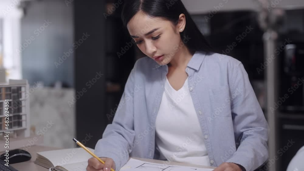 Dedicated Asian female architect diligently examines green print ...