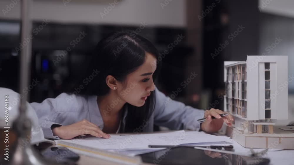Asian female architect attentively checks models and green print ...