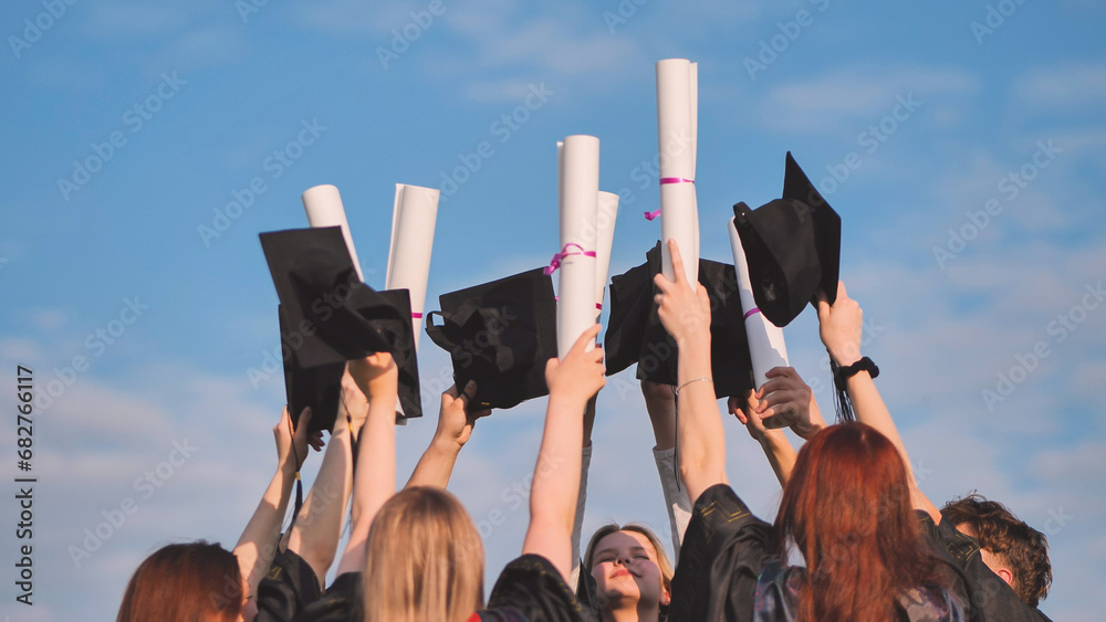 College graduates raise their hands with caps and diplomas to the sky ...