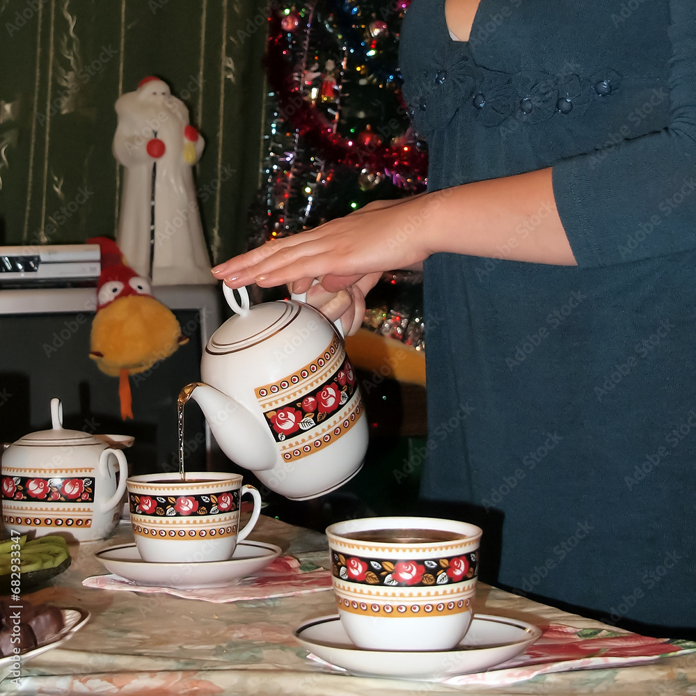 A woman pours tea from a kettle into a cup during a Christmas feast ...