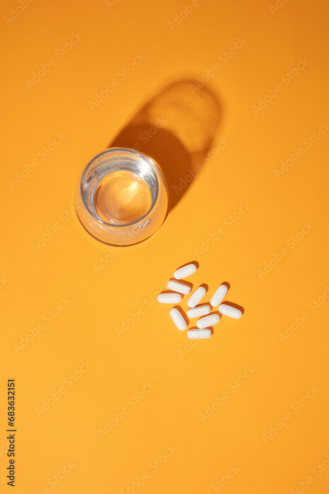 Top view of white tablets placed next to a glass of water on a yellow ...