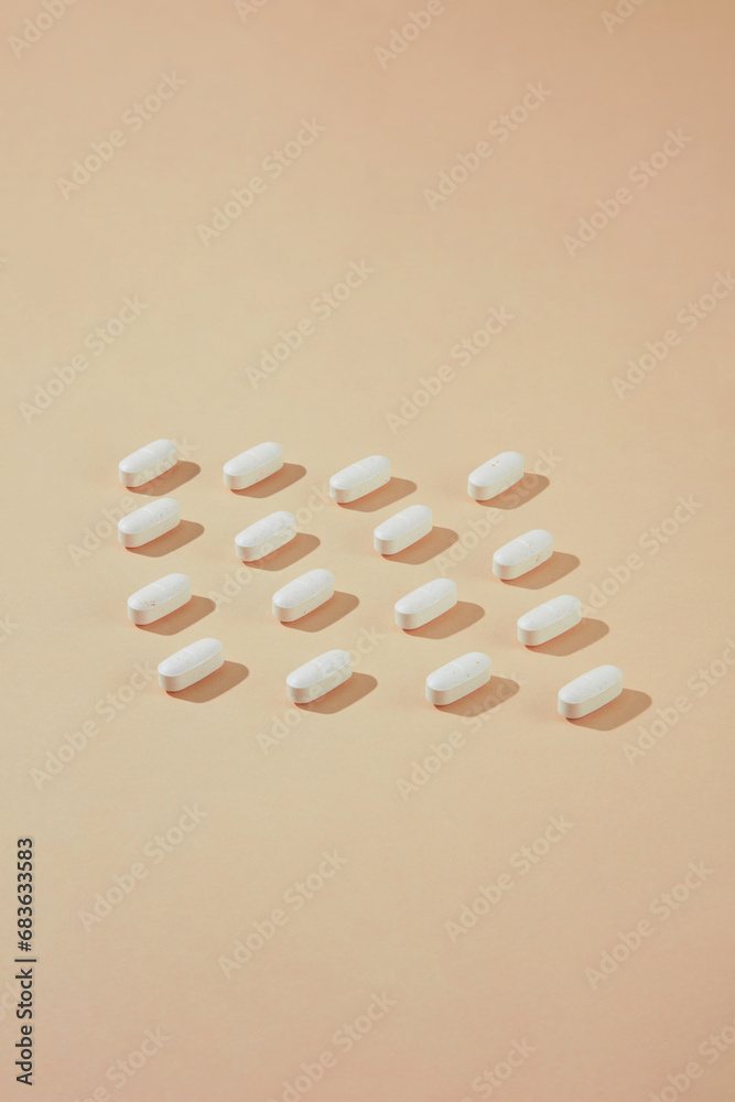 White tablets are arranged evenly on a pastel background. Tablets are ...