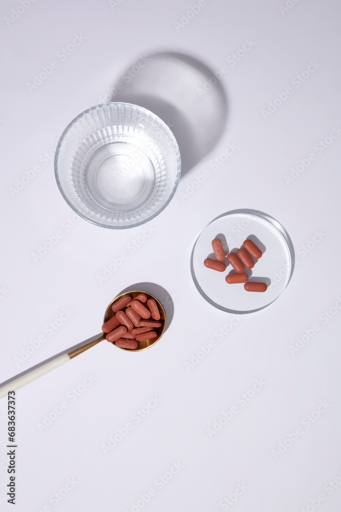 Red tablets placed on a metal spoon and petri dish, a glass of water on ...