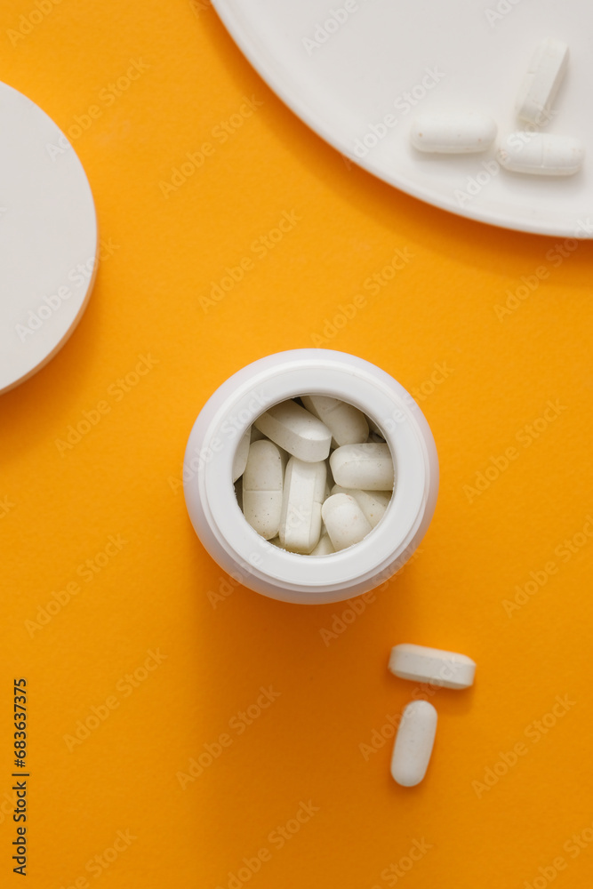 Top view of a plastic bottle filled with white tablets on an orange ...
