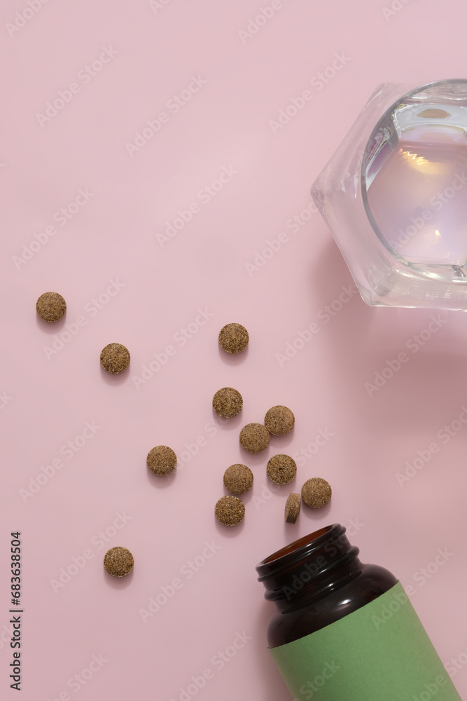 Round brown tablets poured from an unlabeled pill bottle on a pastel ...