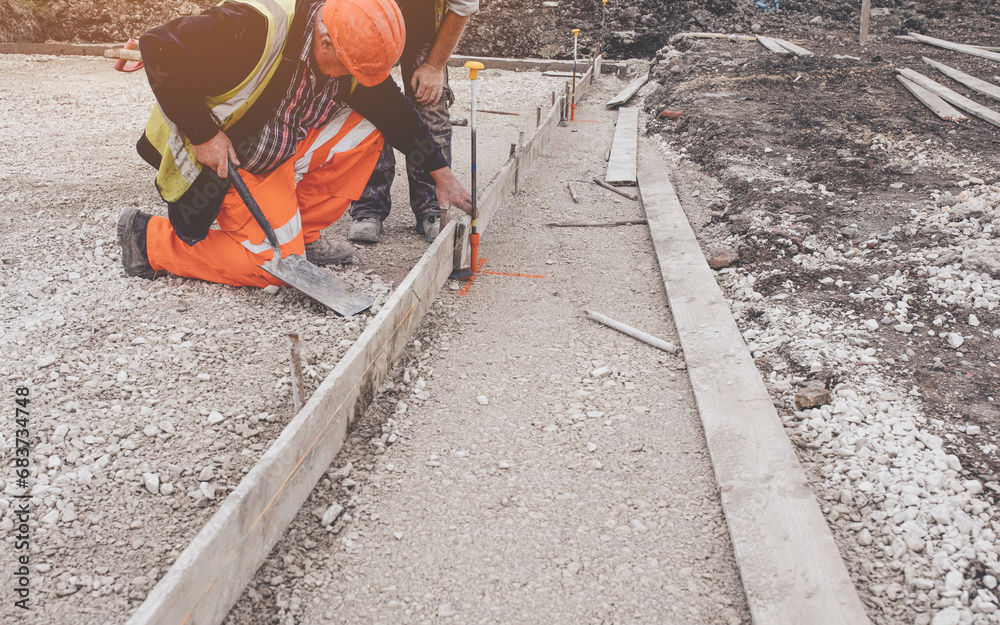 Groundworker in orange safety hi-vis trousers fixing a timber along ...