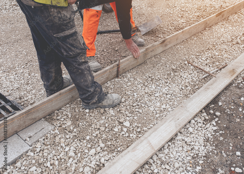 Groundworker in orange safety hi-vis trousers fixing a timber along ...