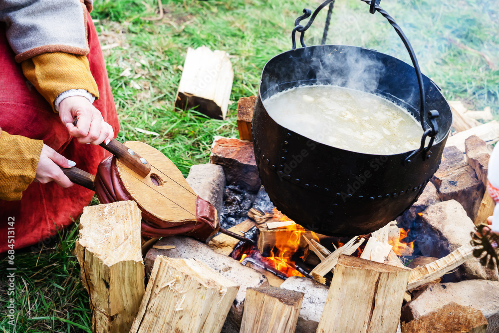 Cooking in medieval style. A woman in national costume starts a fire ...