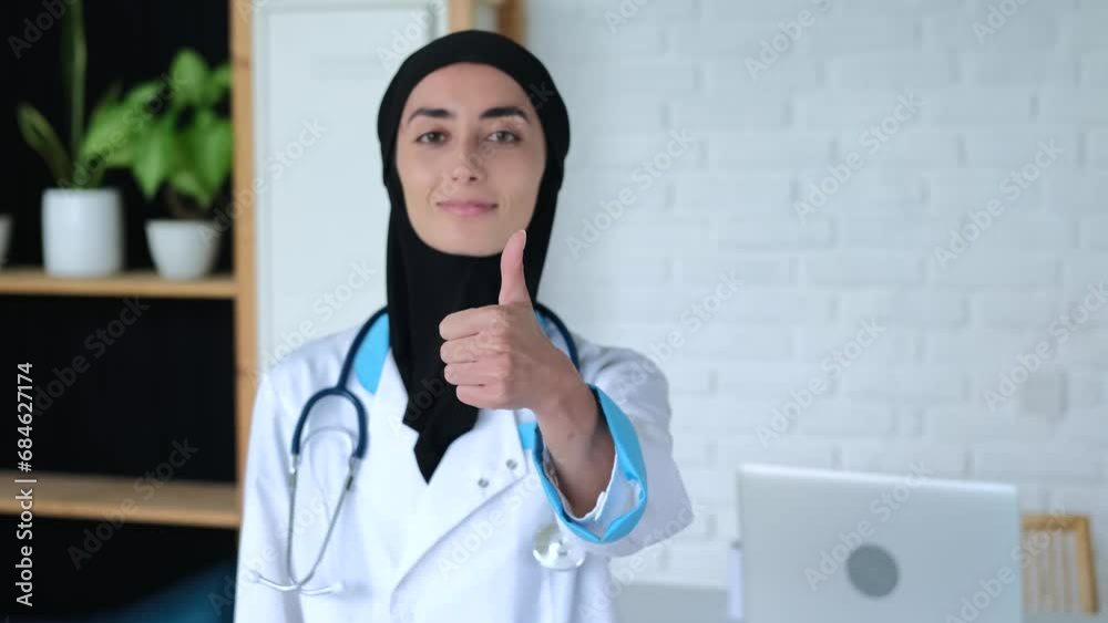 Muslim woman doctor in hijab and uniform with stethoscope showing thumbs up gesture. Doctors ...