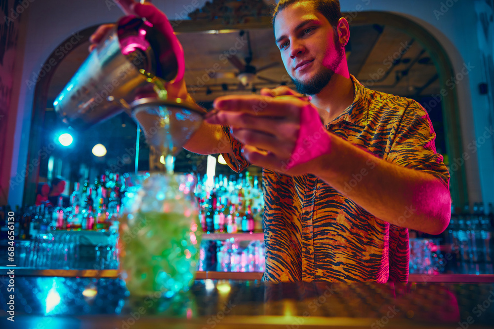 Attractive young bartender gently pouring refreshing mojito from shaker ...
