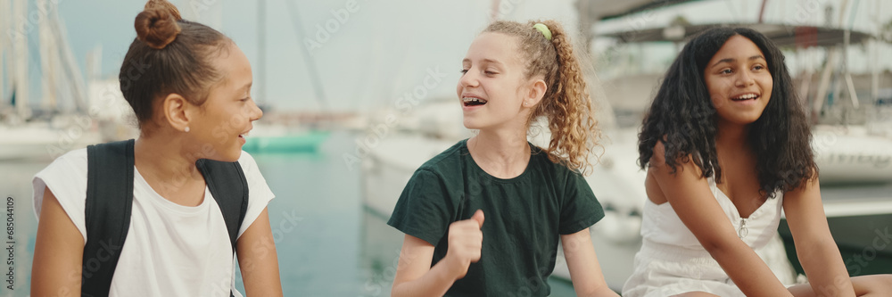 Laughing three girls friends pre-teenage sitting on the waterfront ...