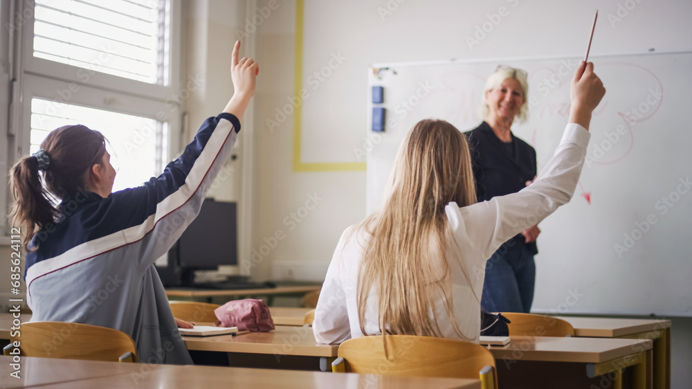 Girl student writes down notes and raises her hand while a female ...