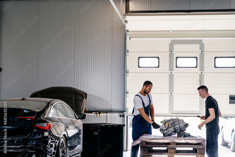 Electric car engine removed from car for repair. Two mechanic men ...