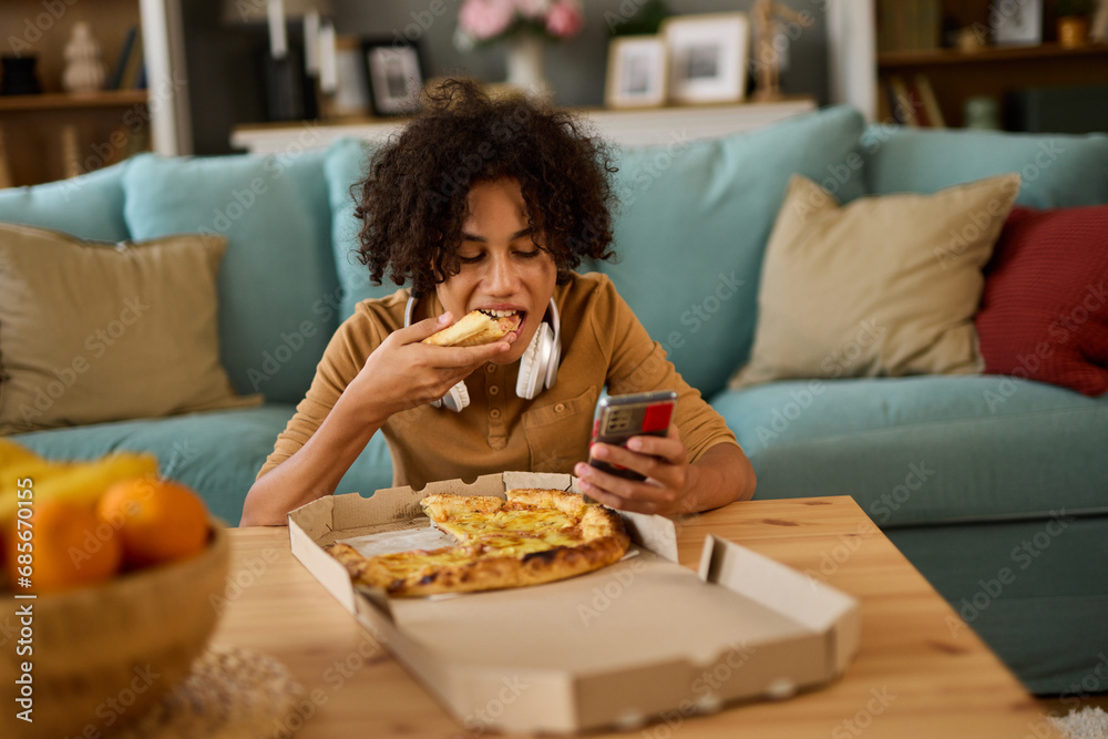 Teenage boy using phone while having pizza at home Stock Photo | Adobe ...