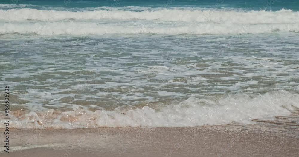 Turquoise sea waves wash sandy shore in sunlight. White sea foam ...