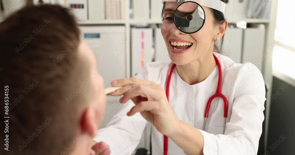 Doctor with frontal reflector on forehead examining throat of male ...