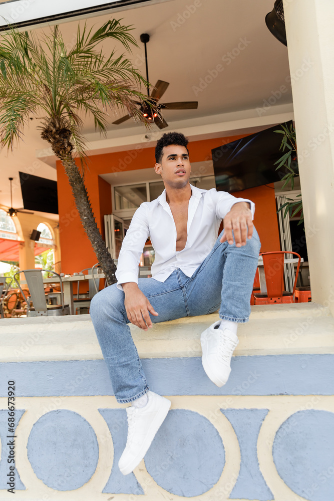 cuban man in white shirt and jeans sitting on parapet of outdoor cafe ...