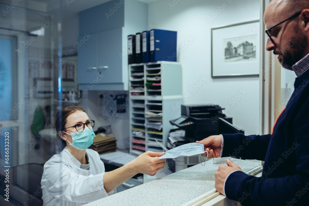 Employee at reception desk of hospital ward handing over mask to ...