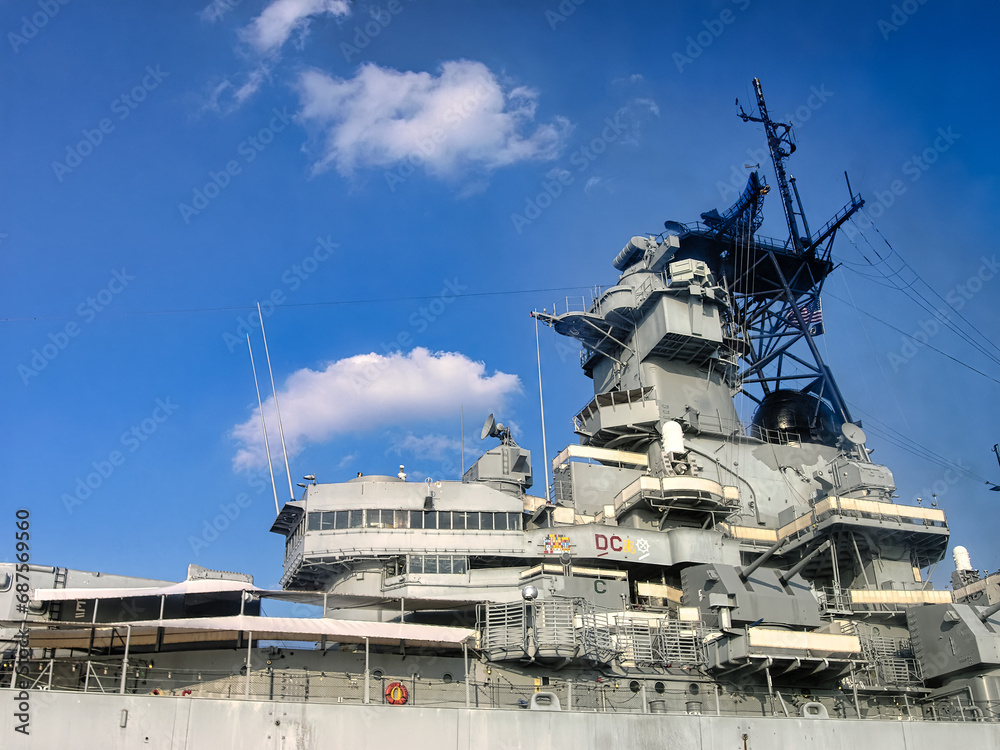 A gray navy ship with large gun turrets and a radar antenna moored at a ...