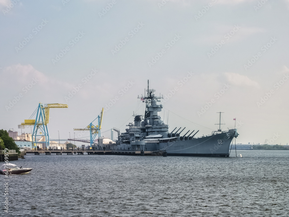 A gray navy battleship with guns and turrets docked at a harbor port ...
