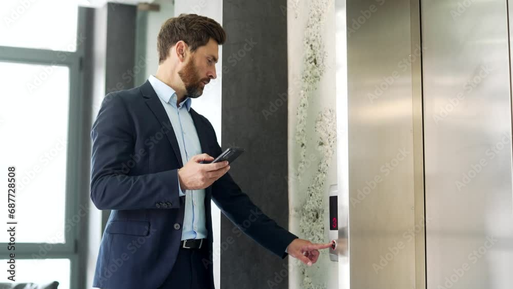Businessman calling the elevator and browsing using a smartphone in a ...